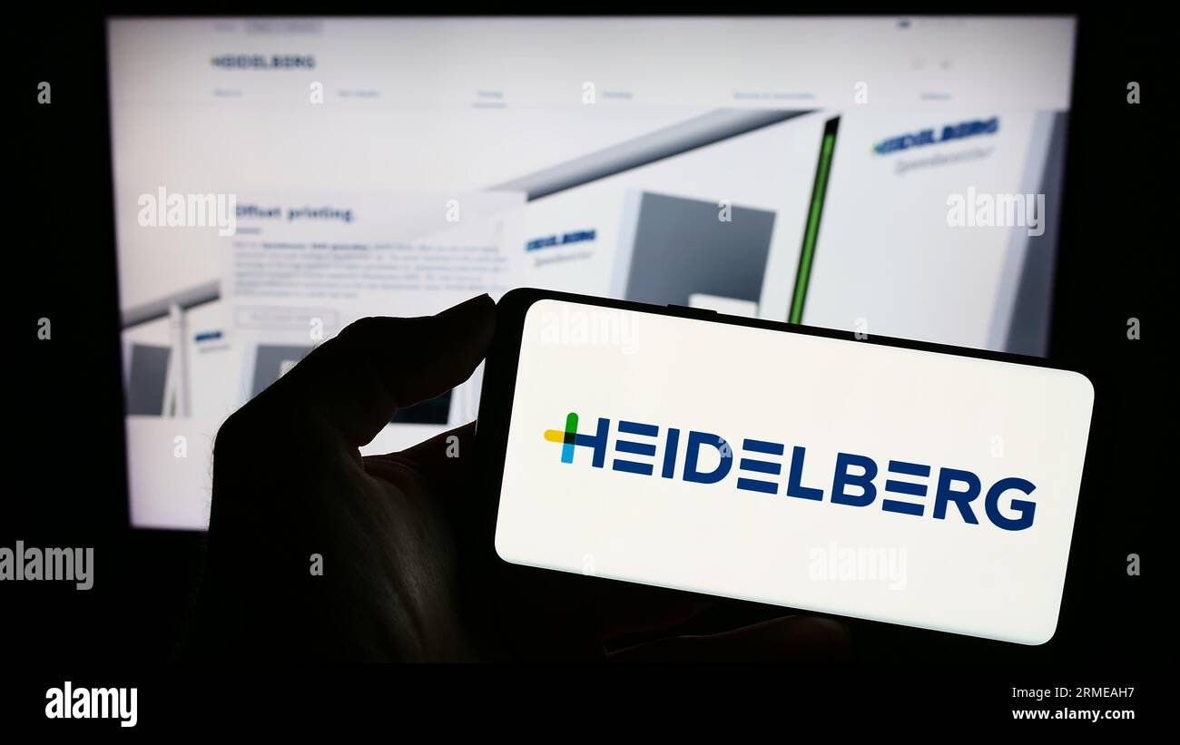 Person holding mobile phone with logo of German company Heidelberger ...