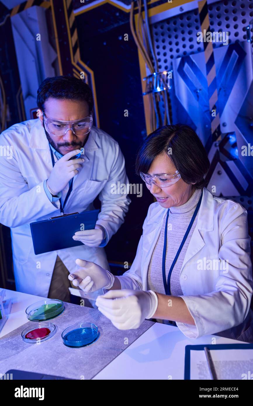 indian scientist with clipboard looking at laboratory glass near ...