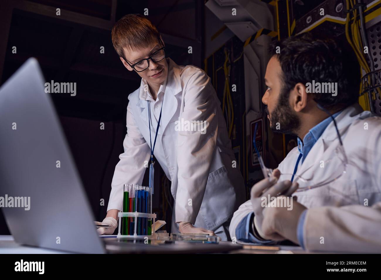 multiethnic scientists talking near laptop and test tubes with alien ...