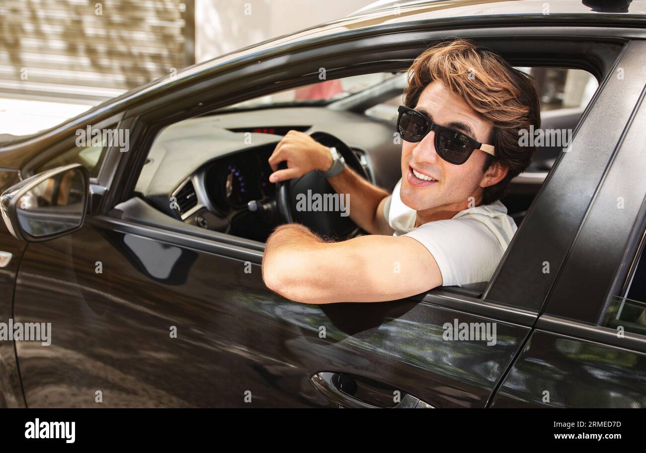 Positive handsome millennial guy wearing sunglasses enjoying car ride ...