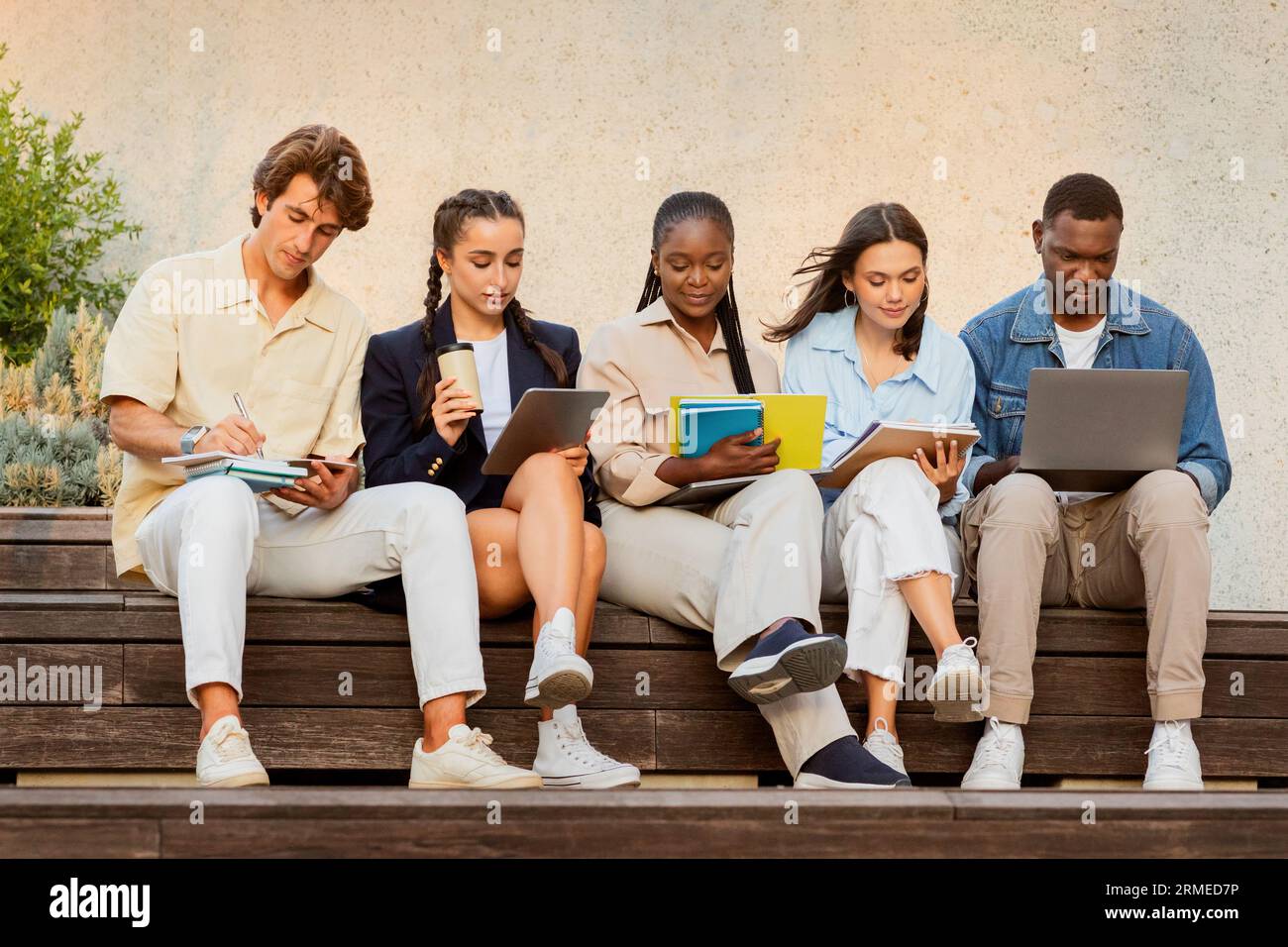 Multiracial group students sitting on bench, getting ready for class ...