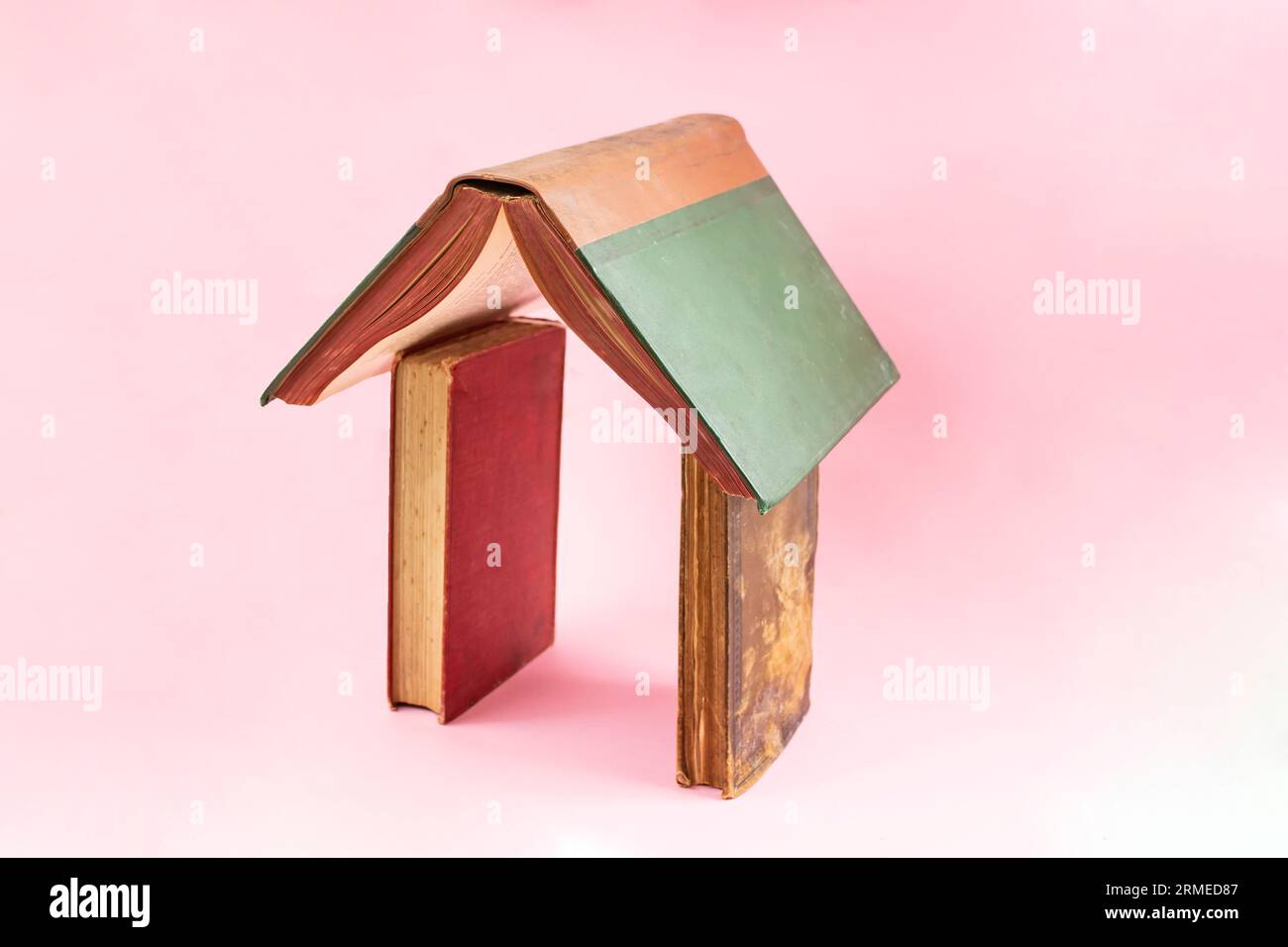 three vintage books arranged in the shape of a house on pink background ...