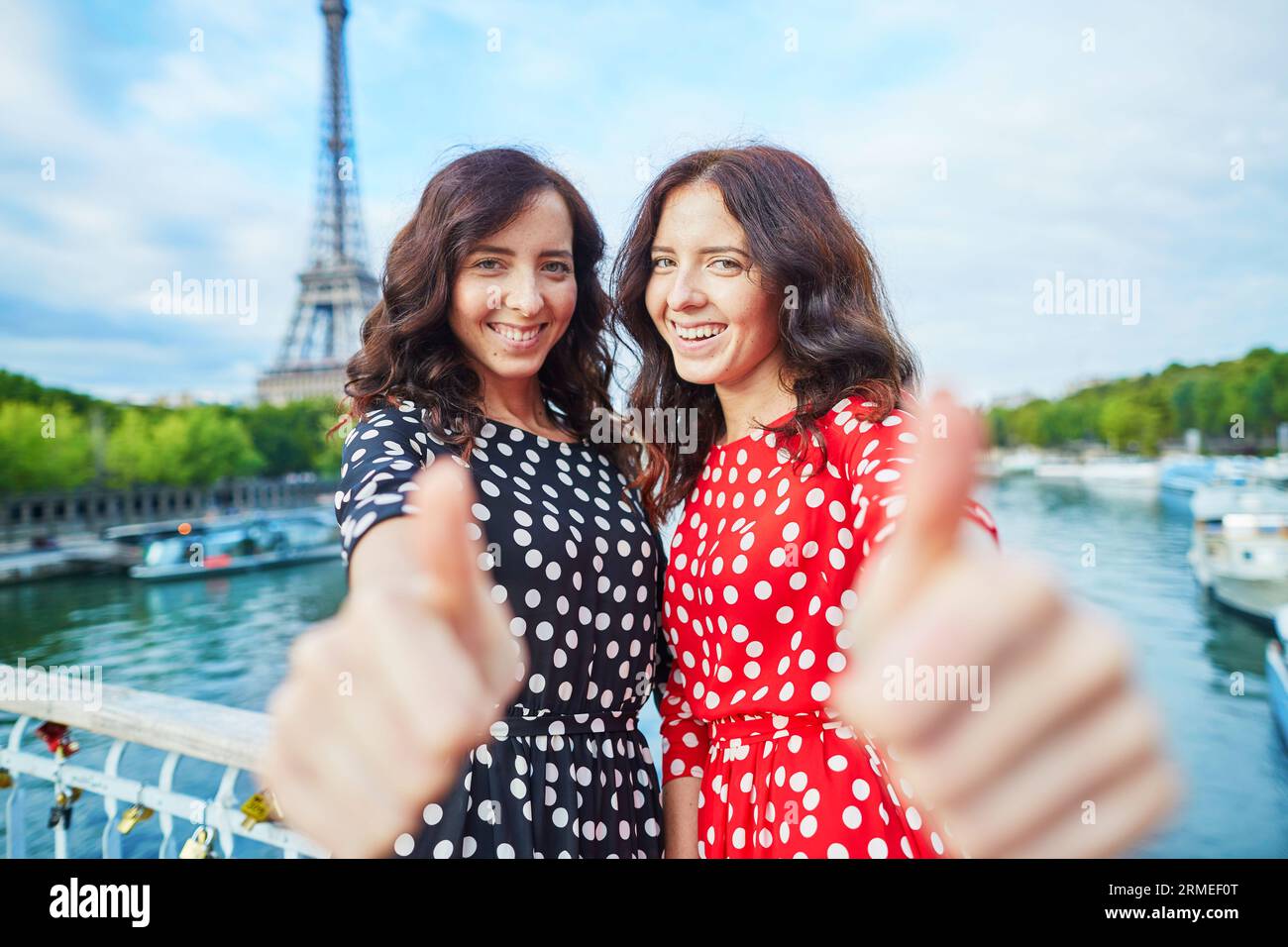 Cheerful smiling twin sisters showing thumbs up success sign in front ...