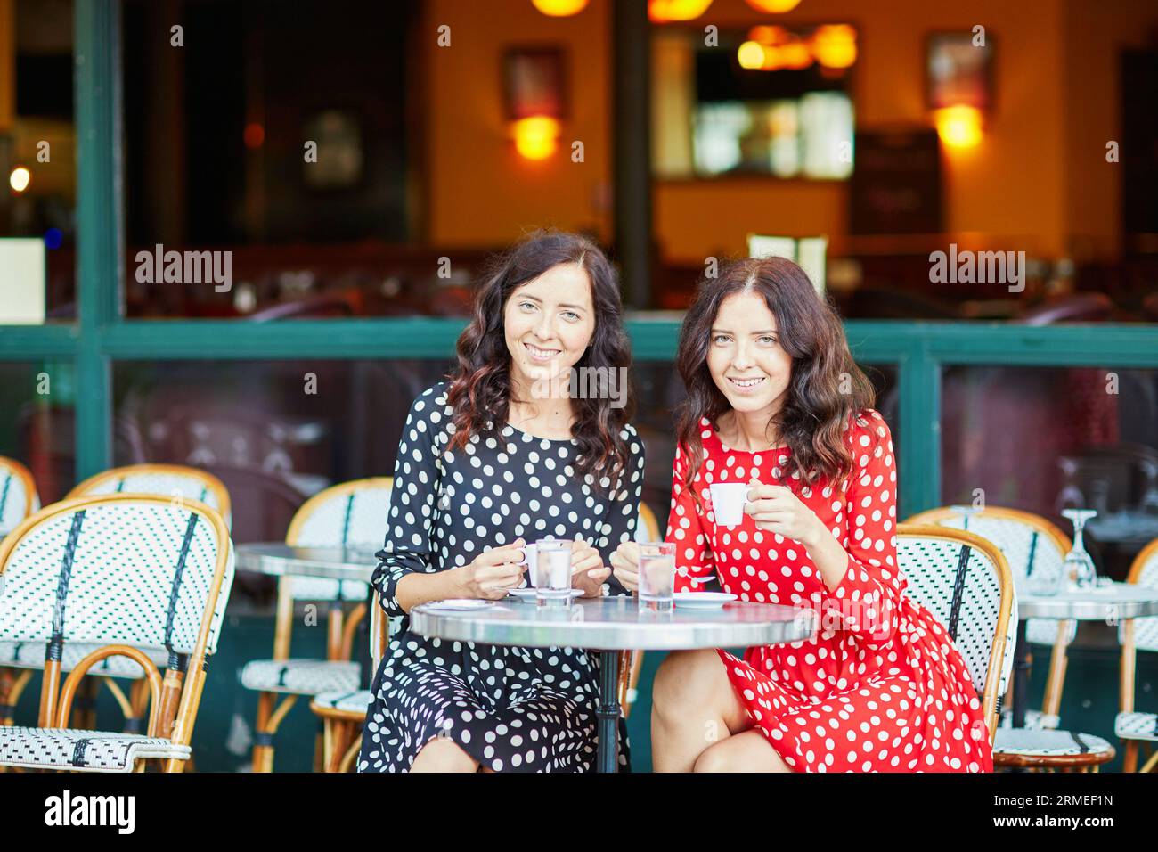 Beautiful twin sisters drinking coffee in a cozy outdoor cafe in Paris ...