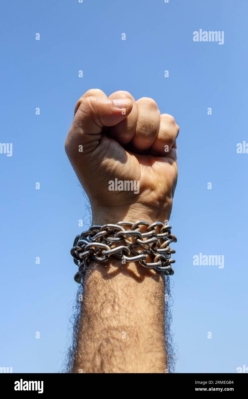 Clenched male fist raised with steel chain tied on the wrist, against ...
