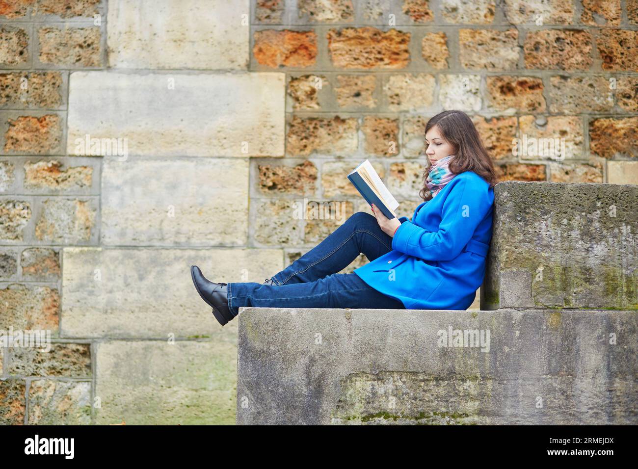 Beautiful young girl reading a book on the Seine embankment in Paris ...
