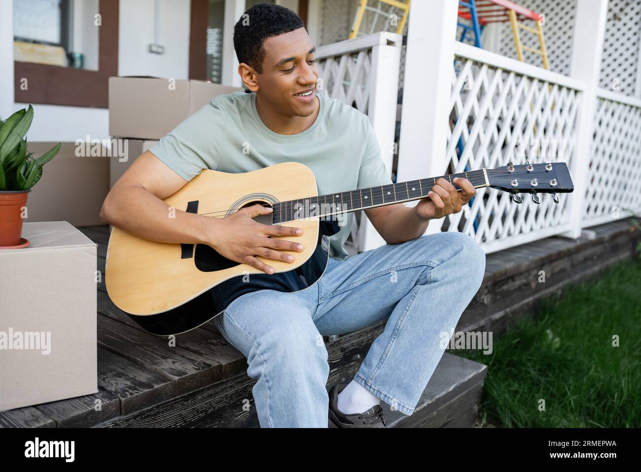 Cheerful African American Man Playing Acoustic Guitar Near Cardboard