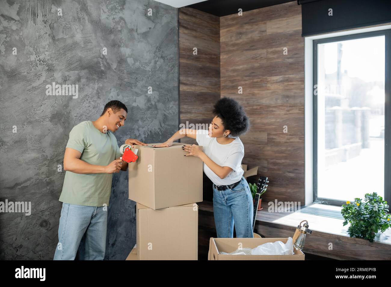 smiling african american couple packaging boxes with adhesive tape ...