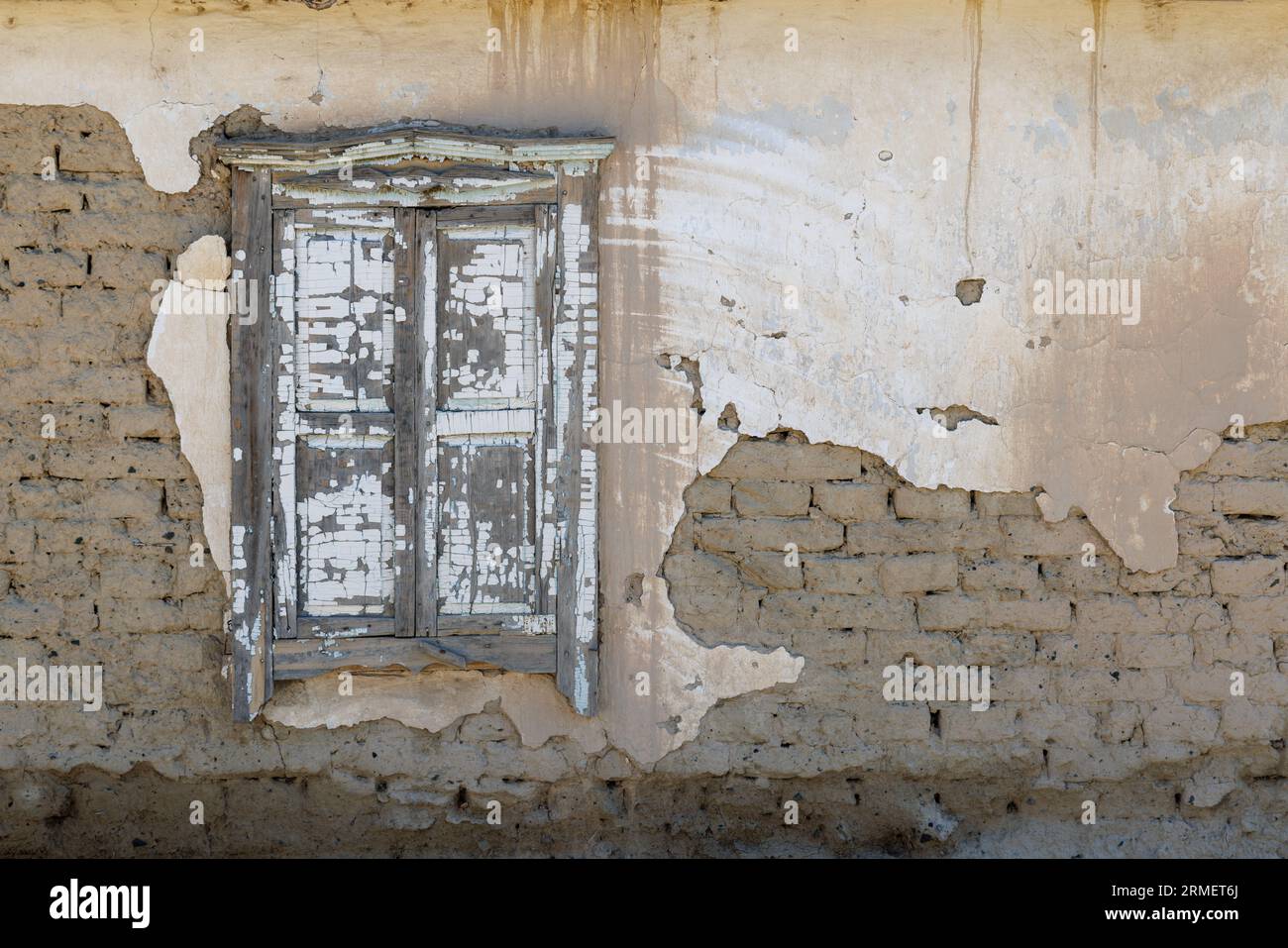 old adobe building wall with old shabby closed wooden window and peeled ...