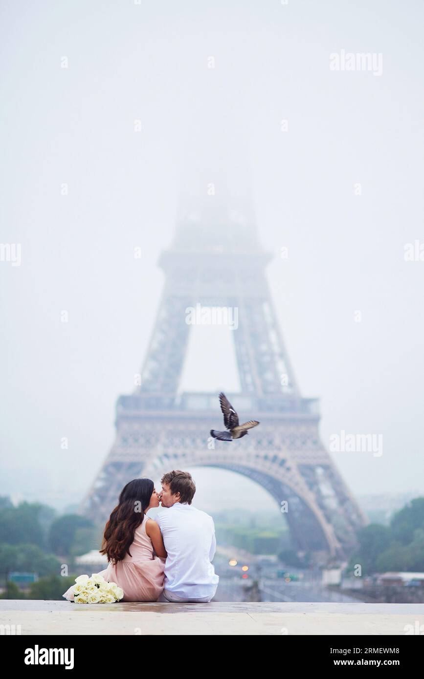 Beautiful romantic couple in love sitting together near the Eiffel tower in Paris on a cloudy ...