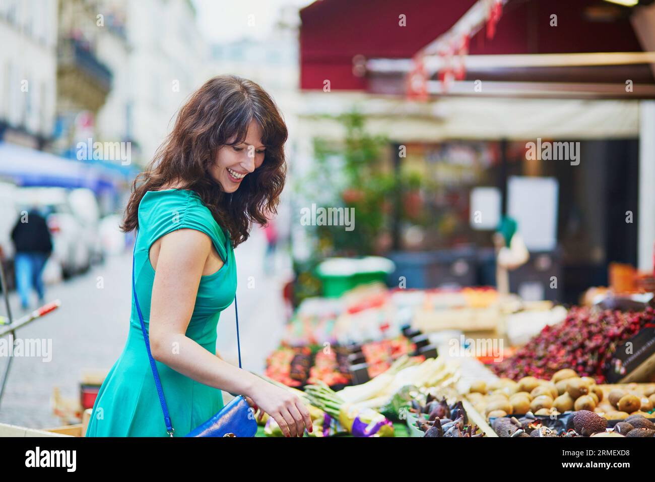 Cheerful happy young French woman selecting fruits on market in Paris ...