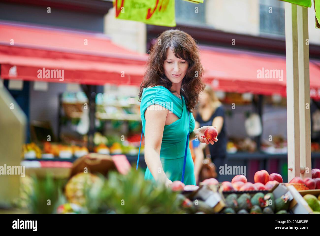 Cheerful happy young French woman selecting peaches on market in Paris ...