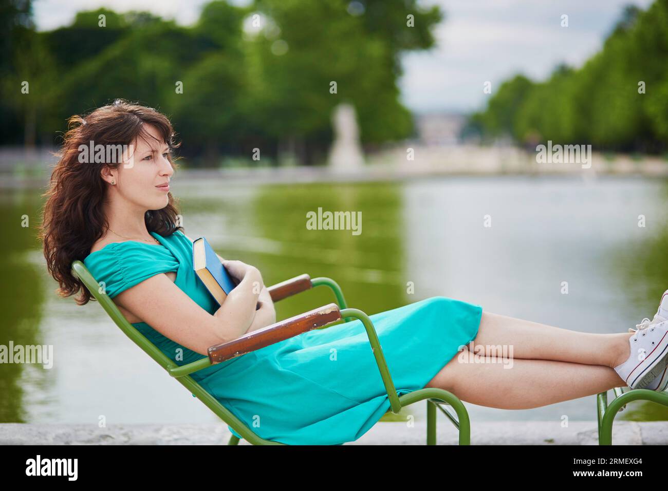 Beautiful young woman in green dress reading a book in Tuileries garden ...
