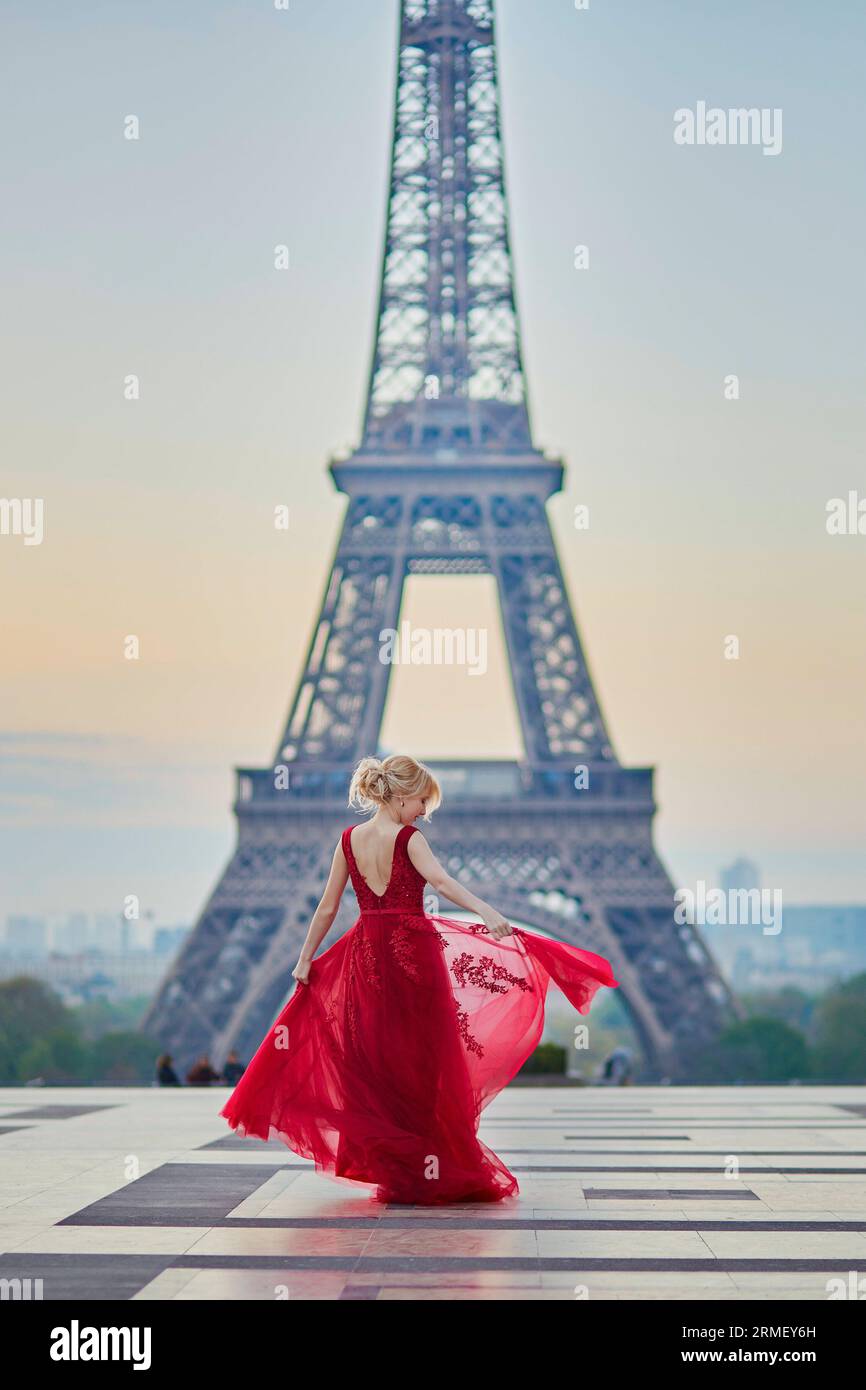 Beautiful young woman in long red dress dancing near the Eiffel tower ...