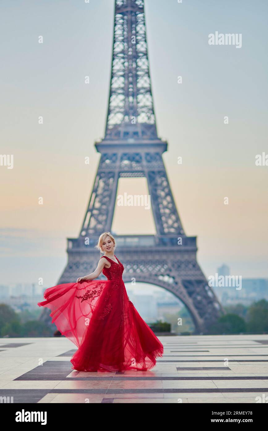 Beautiful young woman in long red dress dancing near the Eiffel tower ...