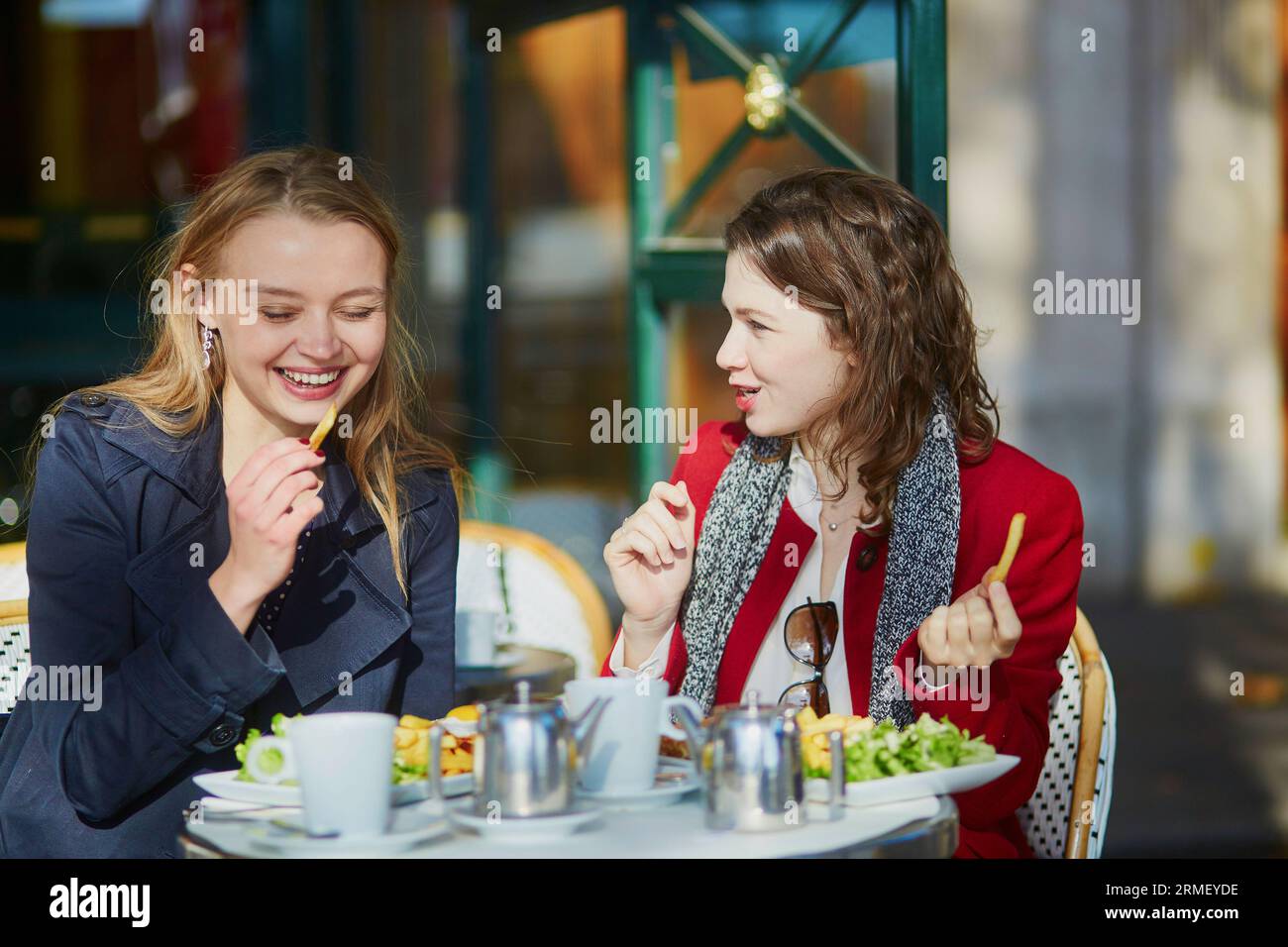 Two young girls in Parisian outdoor cafe, eating French fries ...