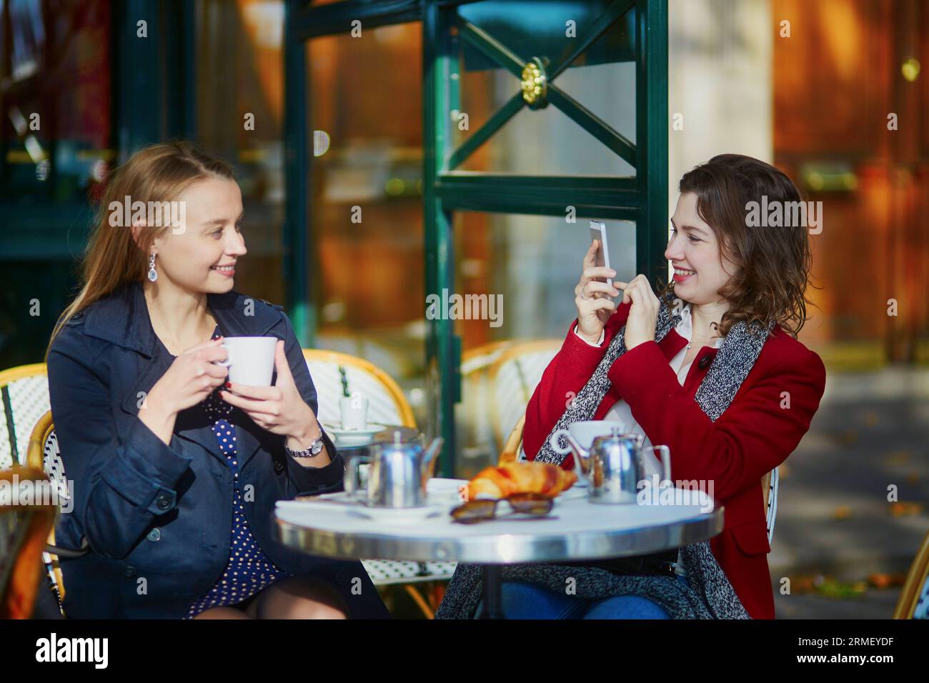 Two girls in outdoor cafe drinking coffee and using mobile phone in ...