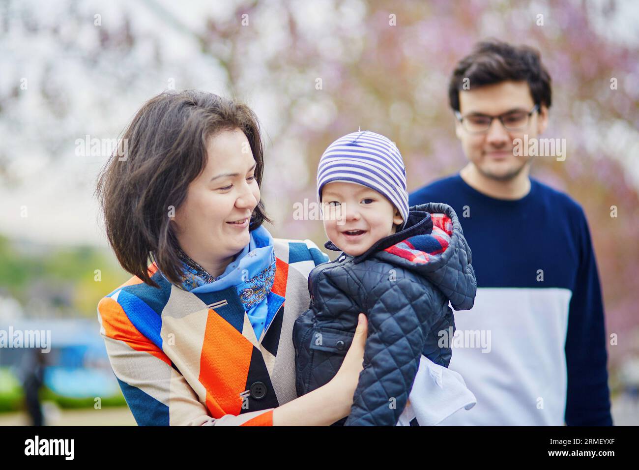 Happy family of three in Paris on a spring day with purple jacarandas ...