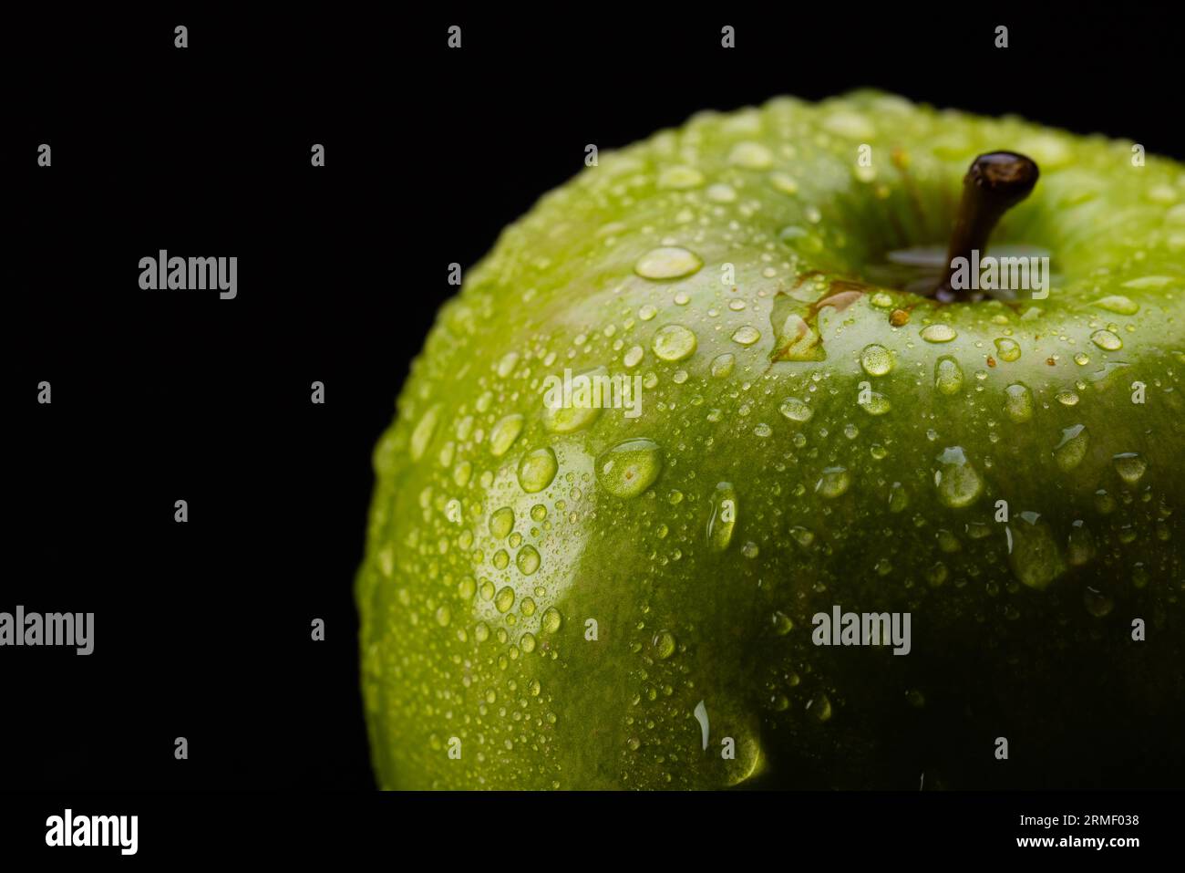 Micro close up of green apple with water drops and copy space on black ...