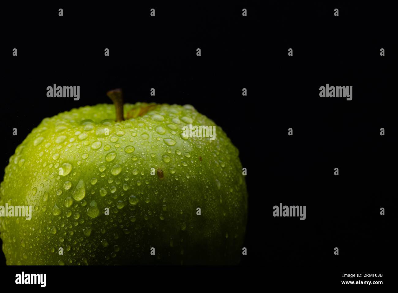 Micro close up of green apple with water drops and copy space on black ...