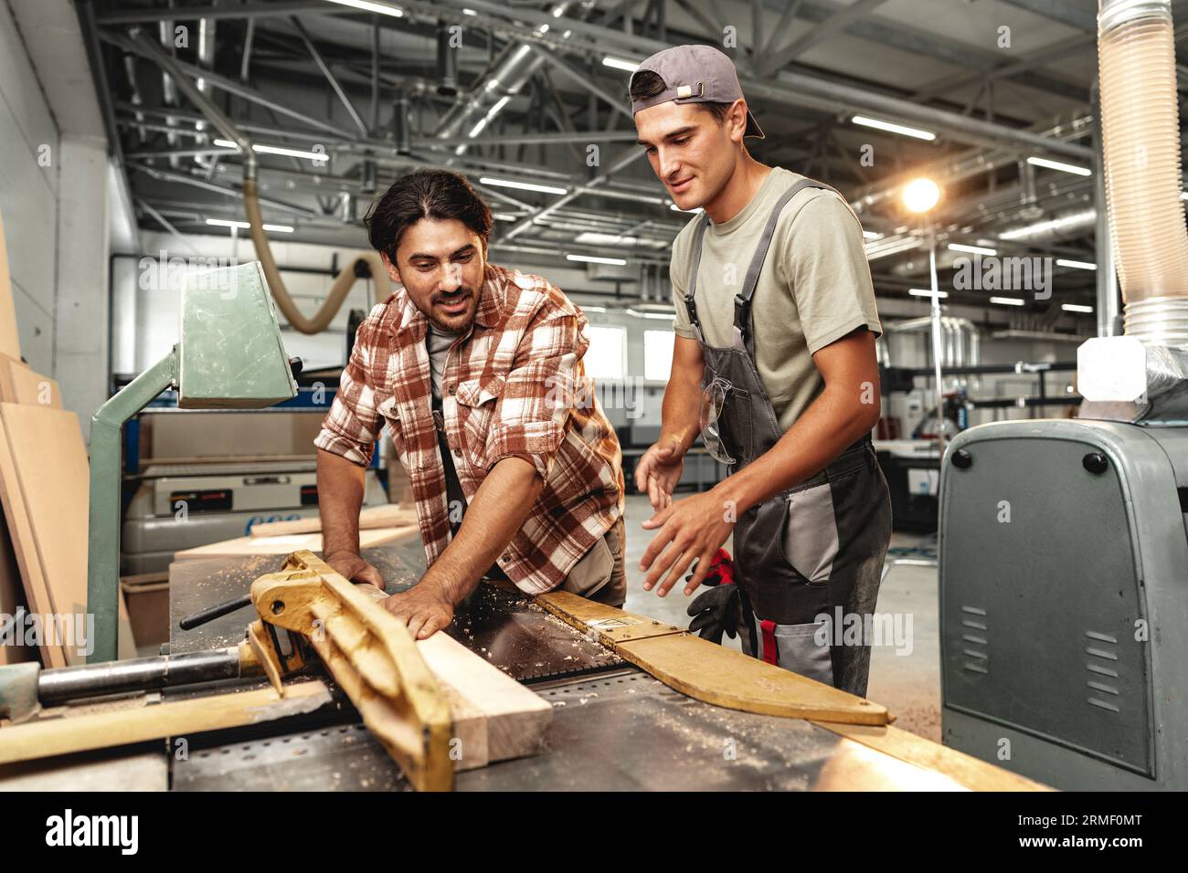 Two young carpenters working with wood standing at table in workshop ...