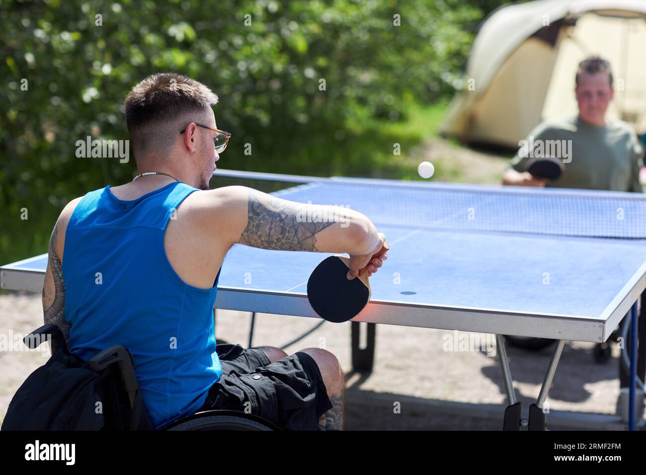 Back view of tattooed man with disabilty playing table tennis with ...
