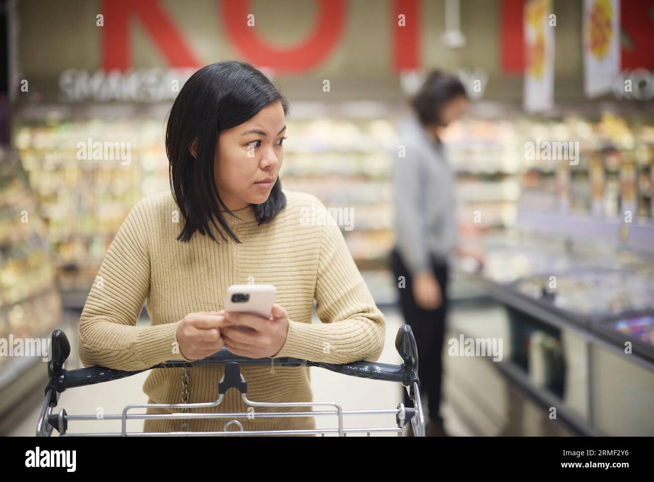 Woman doing shopping in supermarket and holding cell phone Stock Photo ...