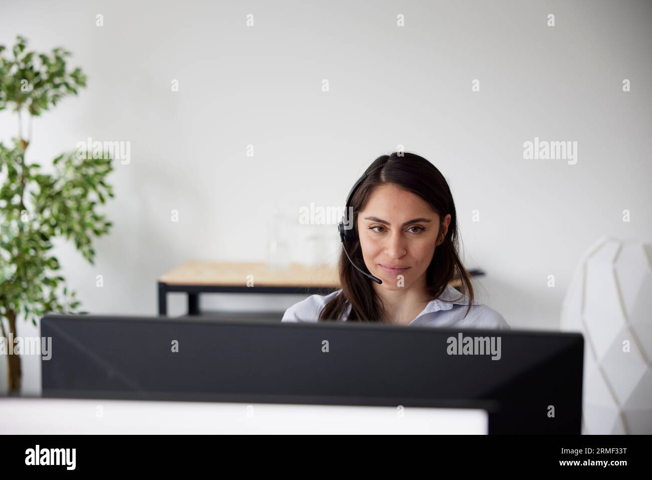 Smiling mid adult businesswoman using headset in office in front of ...