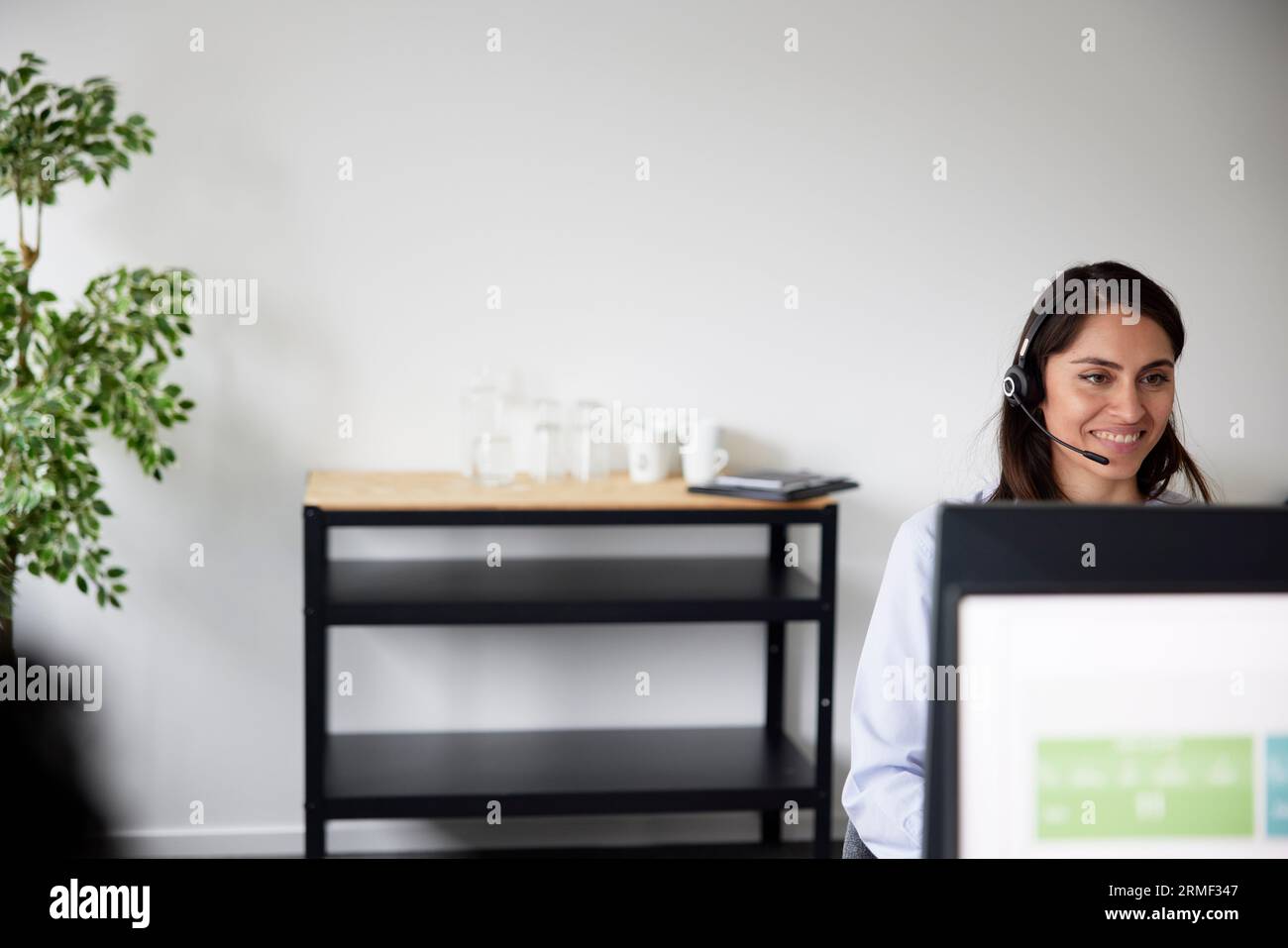 Smiling mid adult businesswoman using headset in office in front of ...