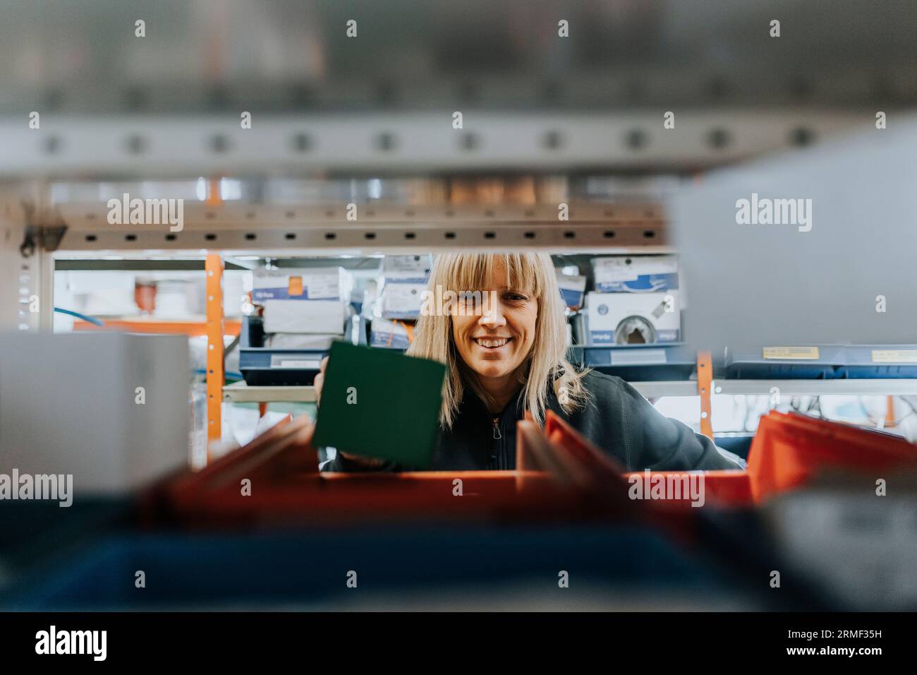 Portrait of smiling female worker taking equipment from shelf Stock ...