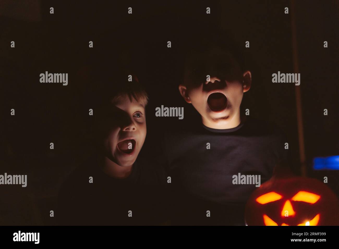 Little boys making scary faces by light og jack-o-lantern. Candle lame ...
