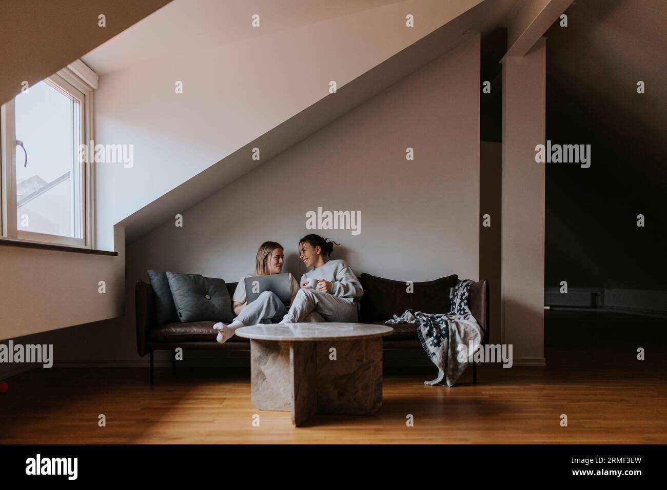 Female couple sitting together on sofa and smiling Stock Photo - Alamy