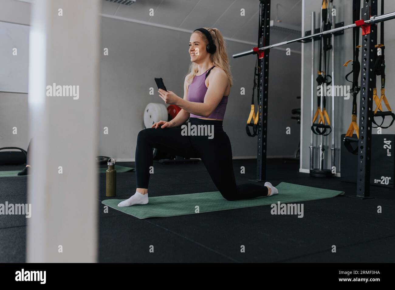 Young woman using phone while stretching on mat in gym Stock Photo - Alamy