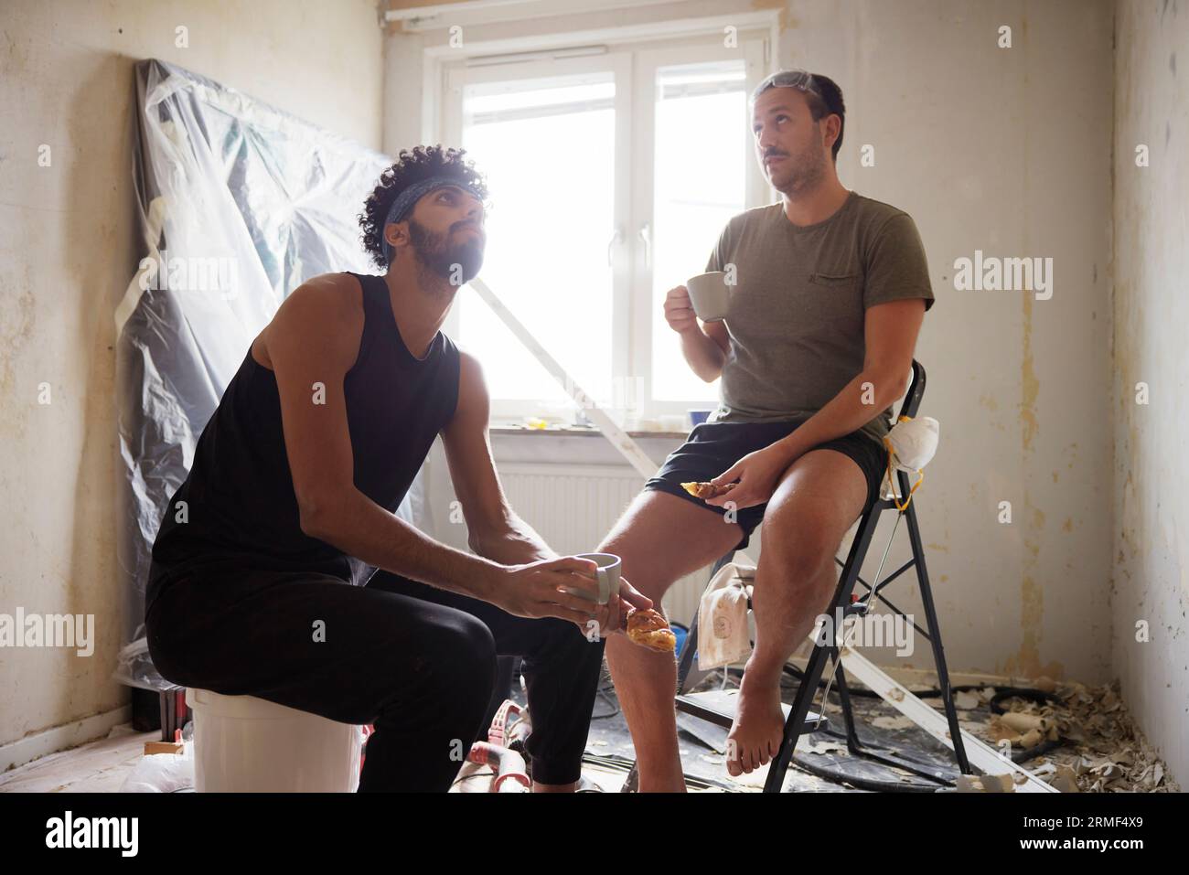 Smiling male homosexual couple having coffee break during apartment ...