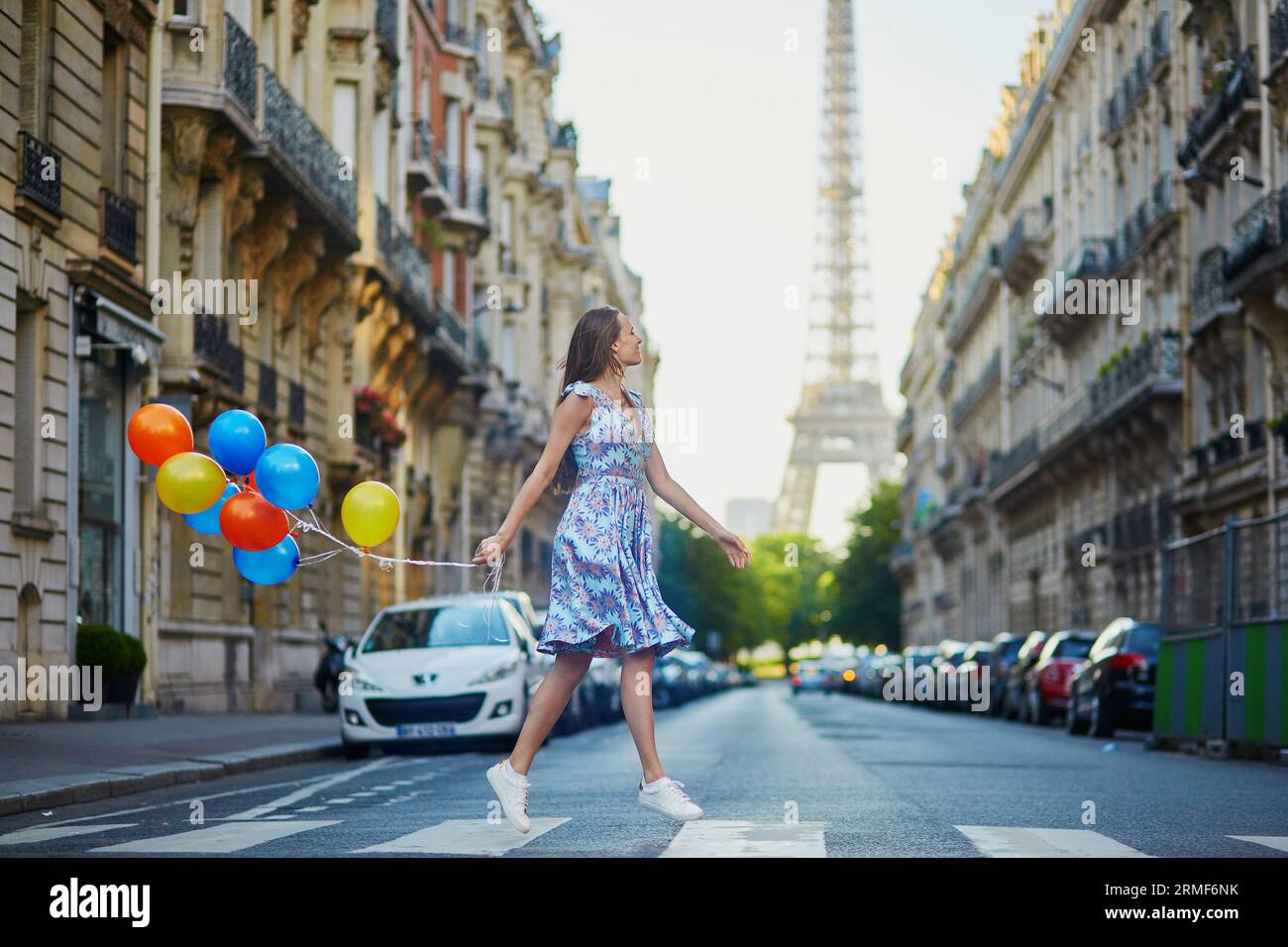 Beautiful young girl with colorful balloons running across the street ...