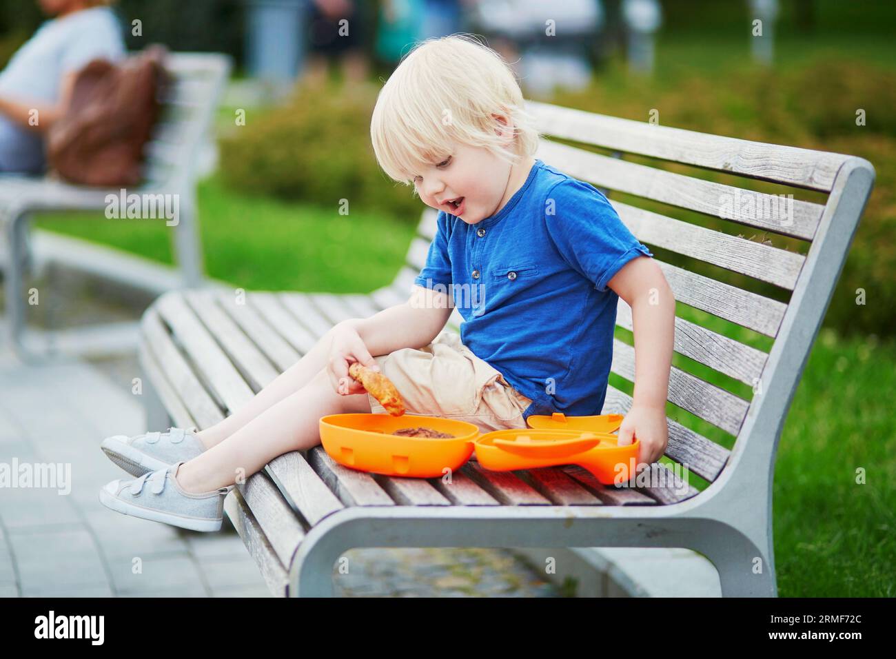Adorable little boy sitting on the bench with lunchbox in park. Healthy ...