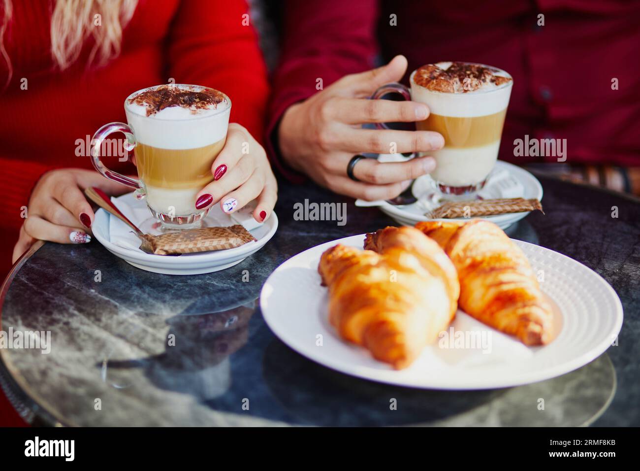 Romantic couple in Parisian outdoor cafe. Tourists drinking coffee and eating croissants in ...