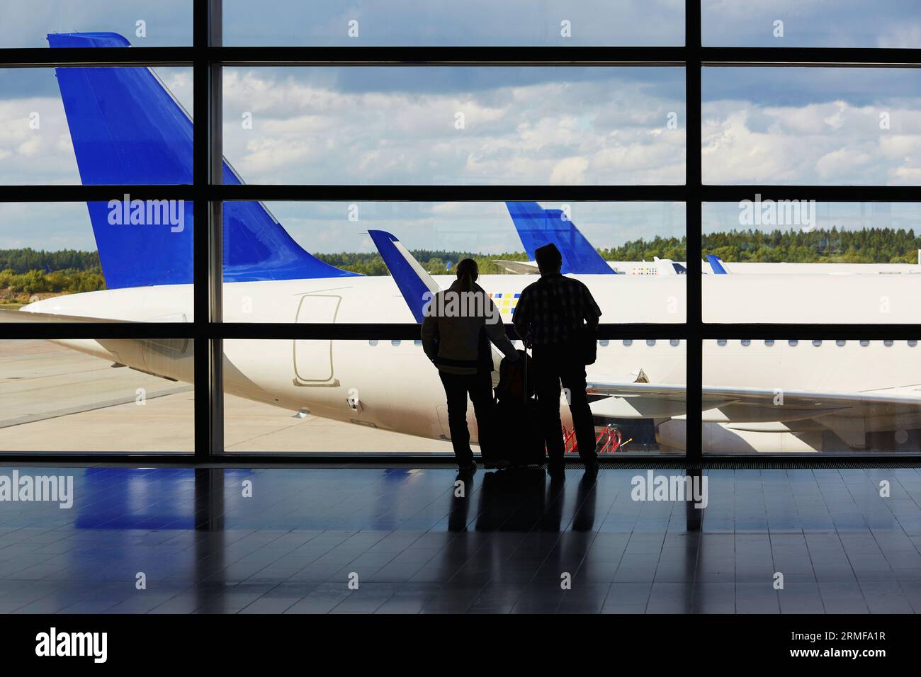 Silhouettes of a couple with hand baggage in the airport, looking at ...
