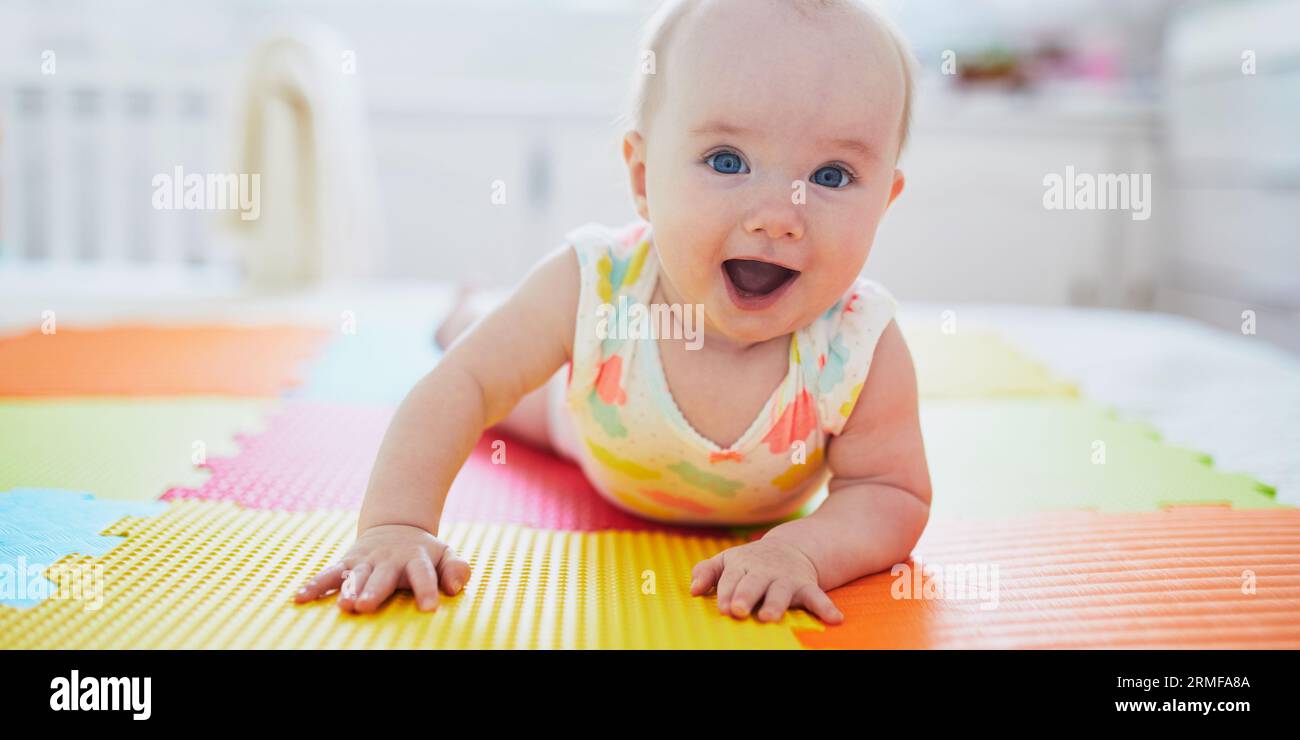 Adorable baby girl doing tummy time on colorful play mat. Happy healthy ...