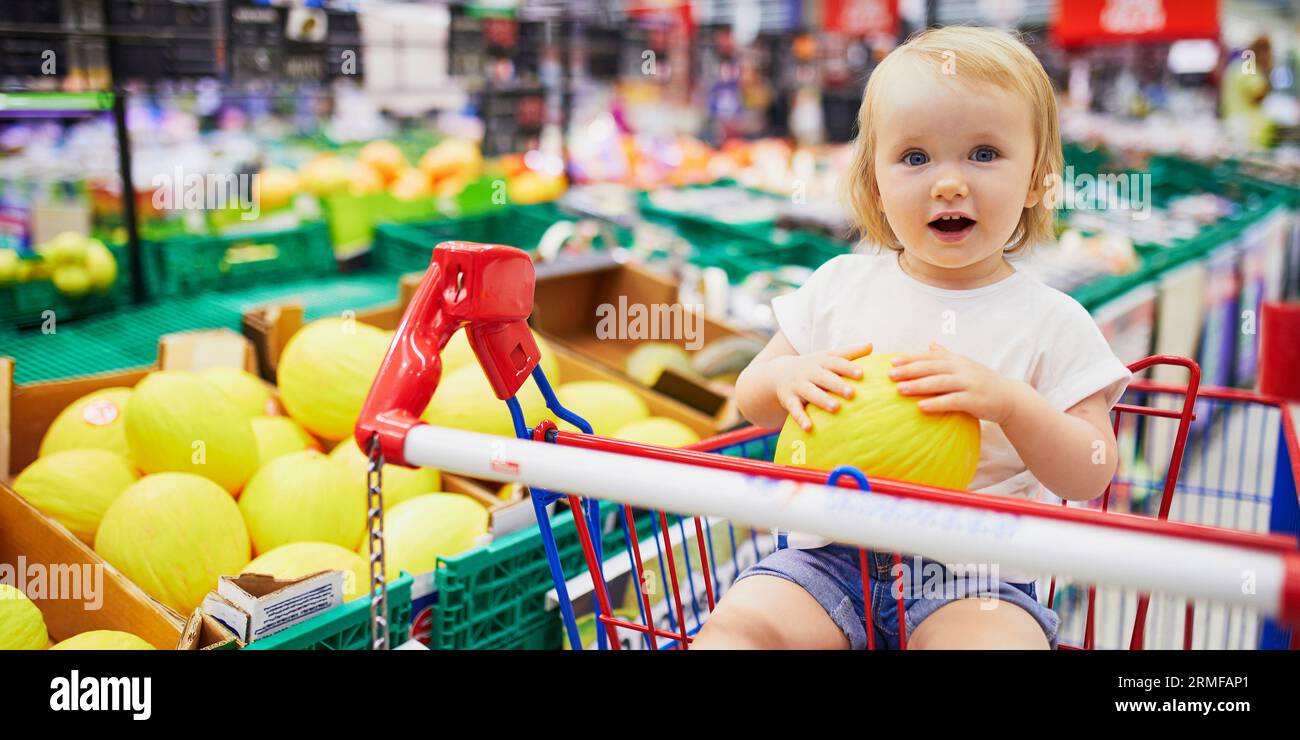 Adorable toddler girl sitting in the shopping cart in a food store or a ...