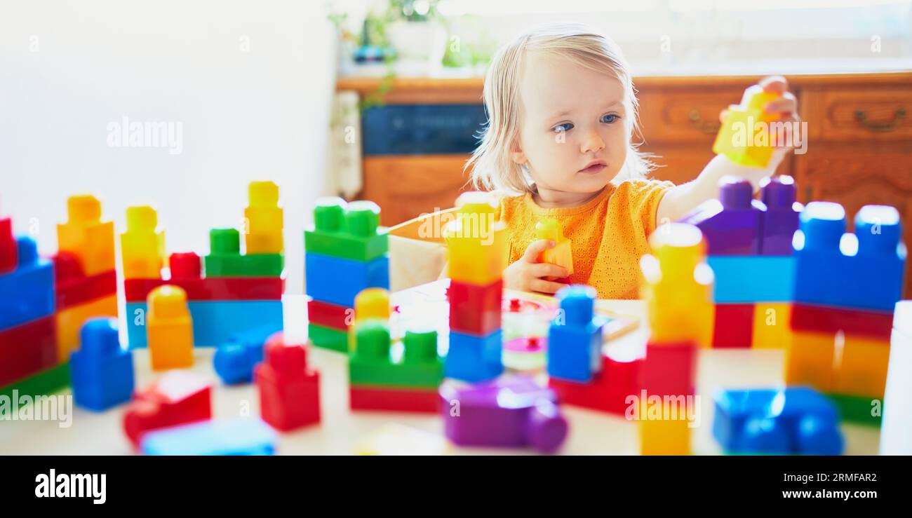 Adorable little girl playing with colorful plastic construction blocks ...