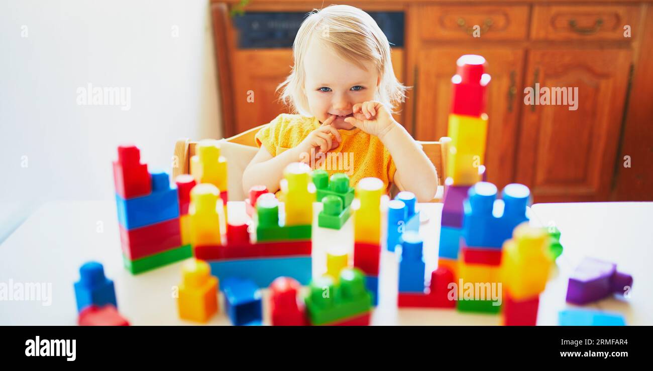 Adorable little girl playing with colorful plastic construction blocks ...