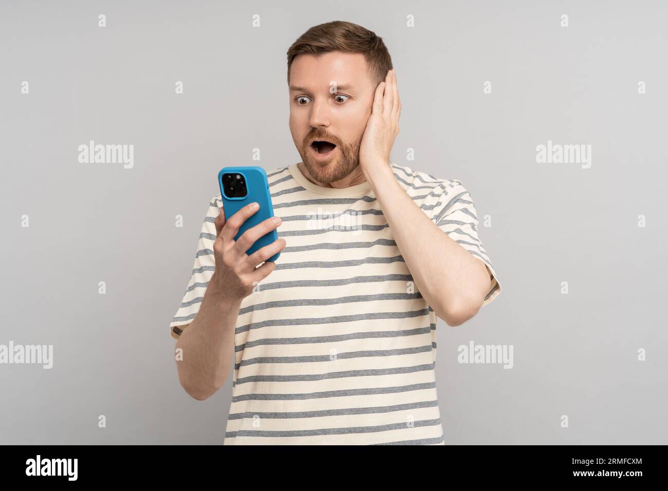 Shocked amazed man looking surprise at screen cellphone touching cheek ...