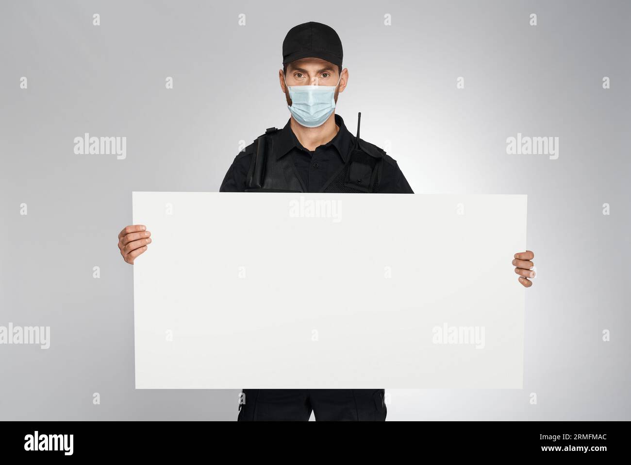 Handsome cop in protective mask holding blank banner, while looking at ...