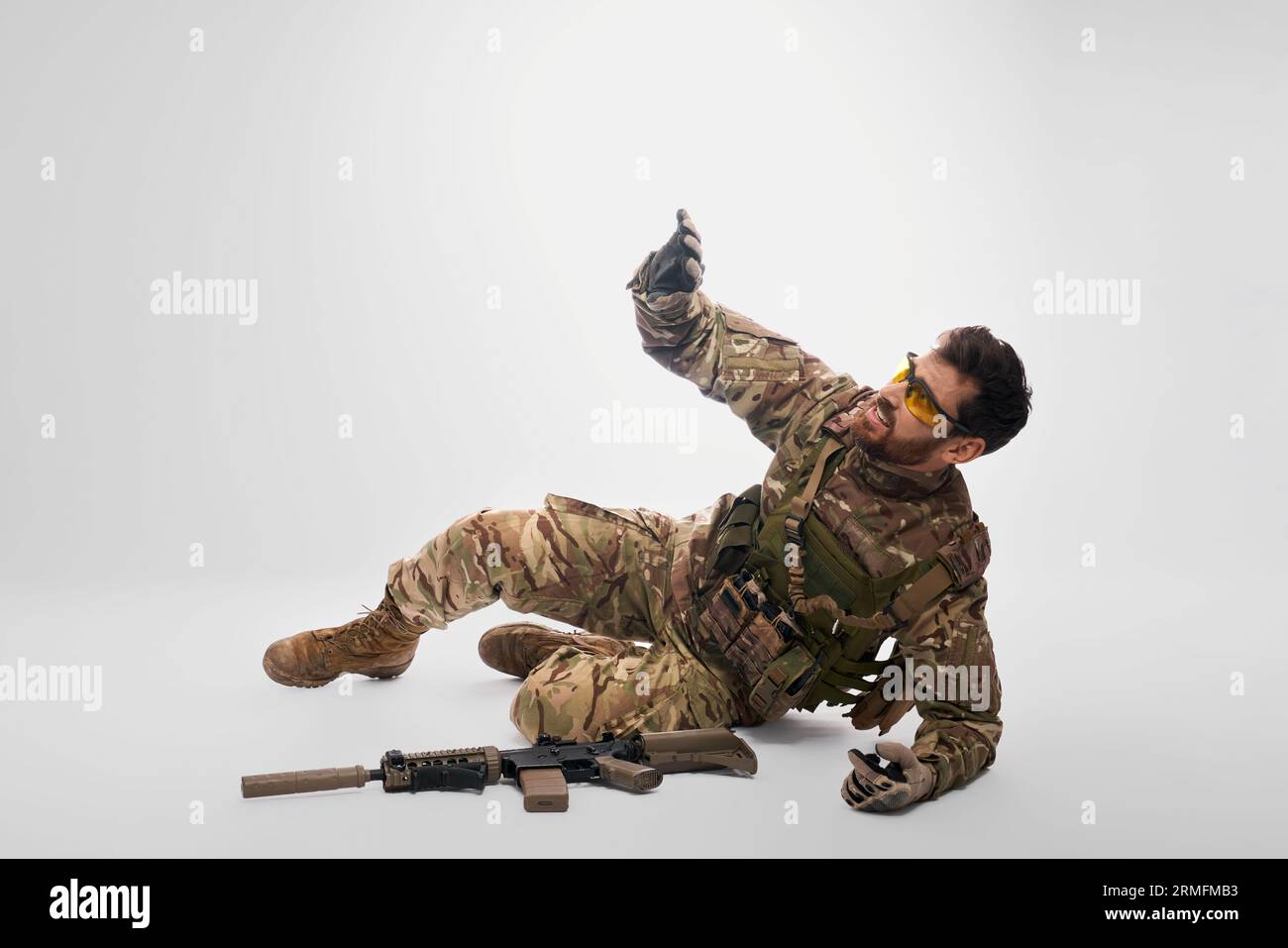 Weak fallen soldier in camouflage asking for help indoors. Side view of ...