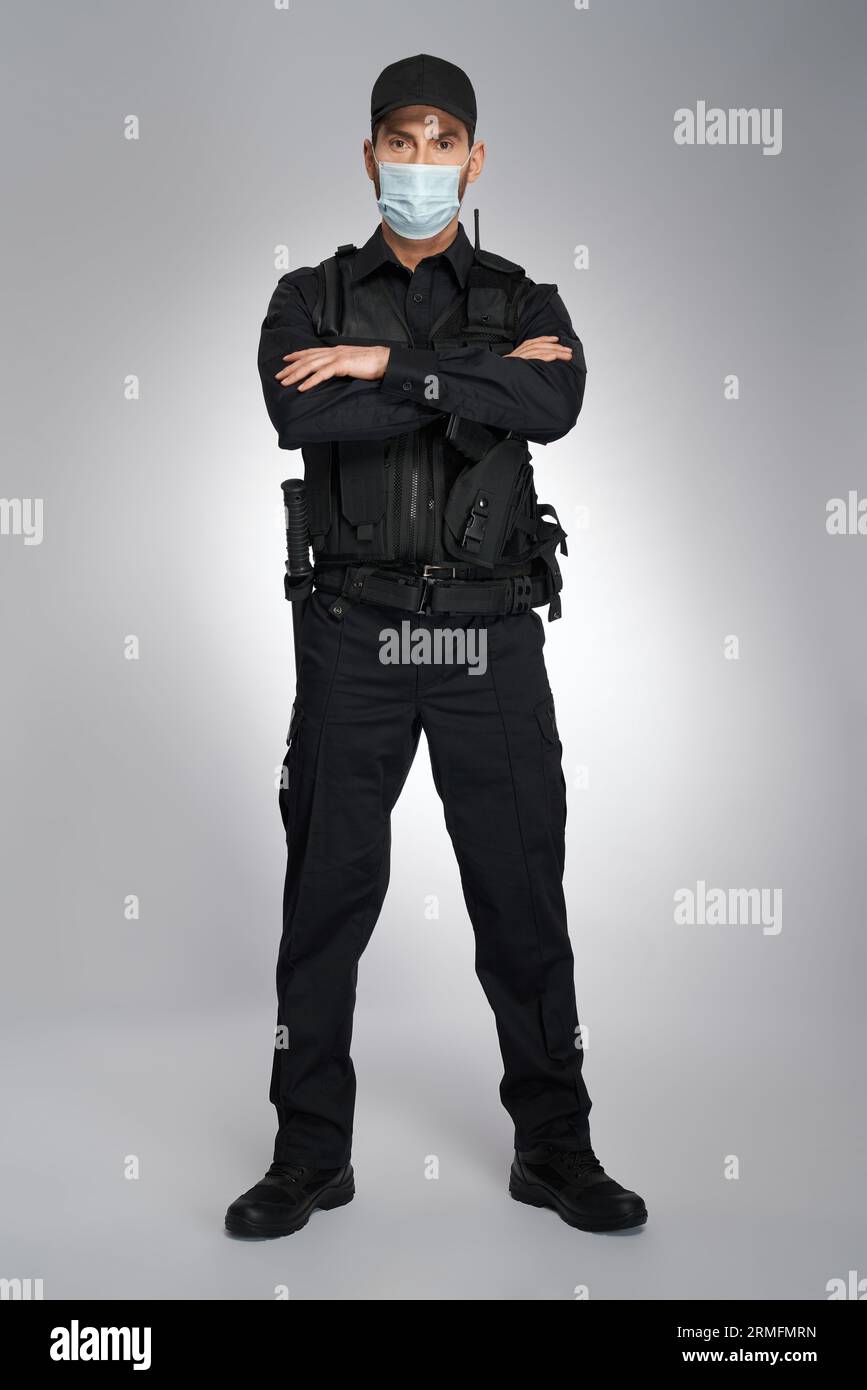 Strong young male cop wearing protective mask looking at camera in ...