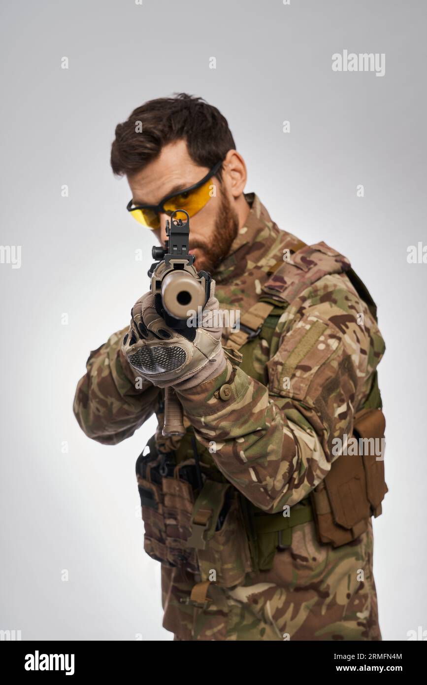 Serious bearded male sniper aiming, by pointing machine gun to camera ...