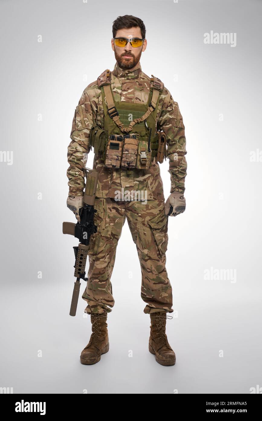 Serious male soldier with rifle in hand, posing in studio. Front view ...