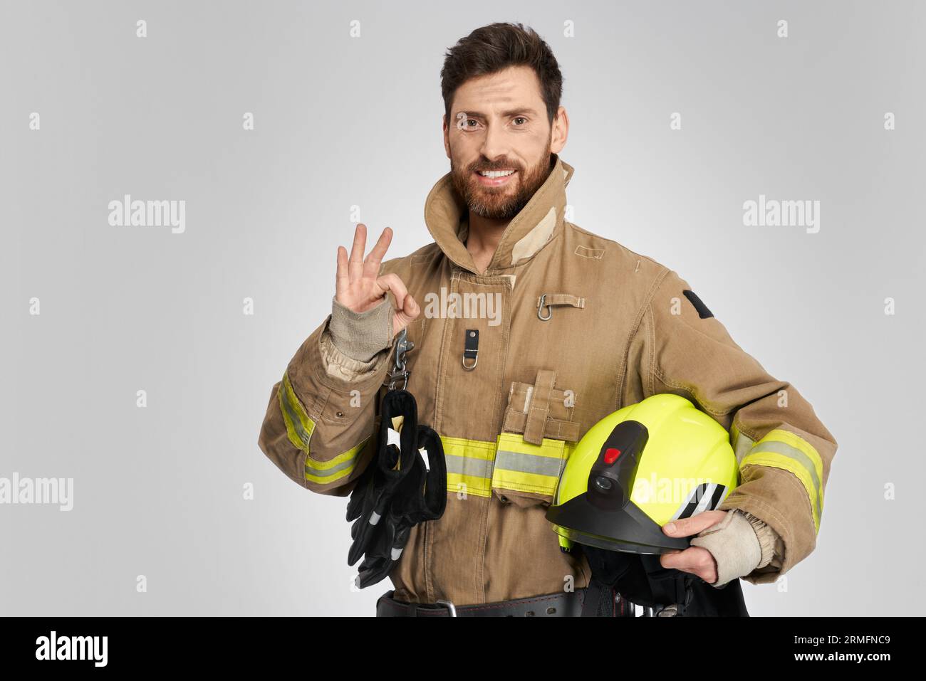 Happy dark-haired firefighter in uniform gesturing okay sign with hand ...