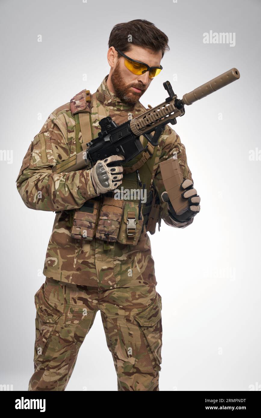 Focused male army soldier in uniform recharging rifle in studio ...